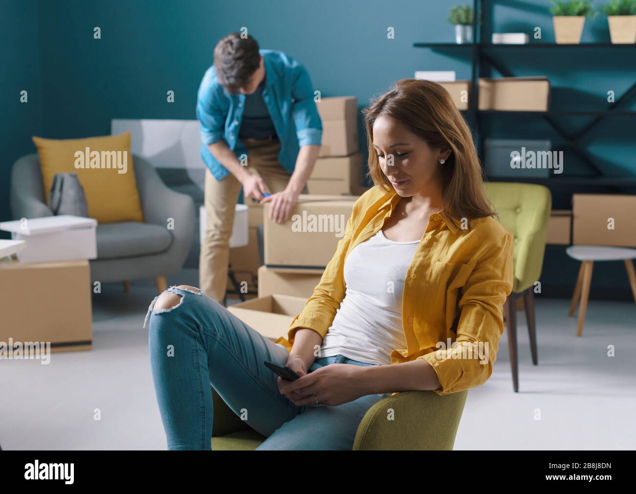 Woman sitting on a chair chatting with her phone during home relocation ...
