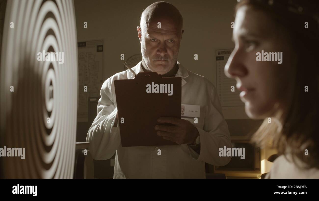 Scientist doing hypnosis experiments in the vintage style lab, a woman ...
