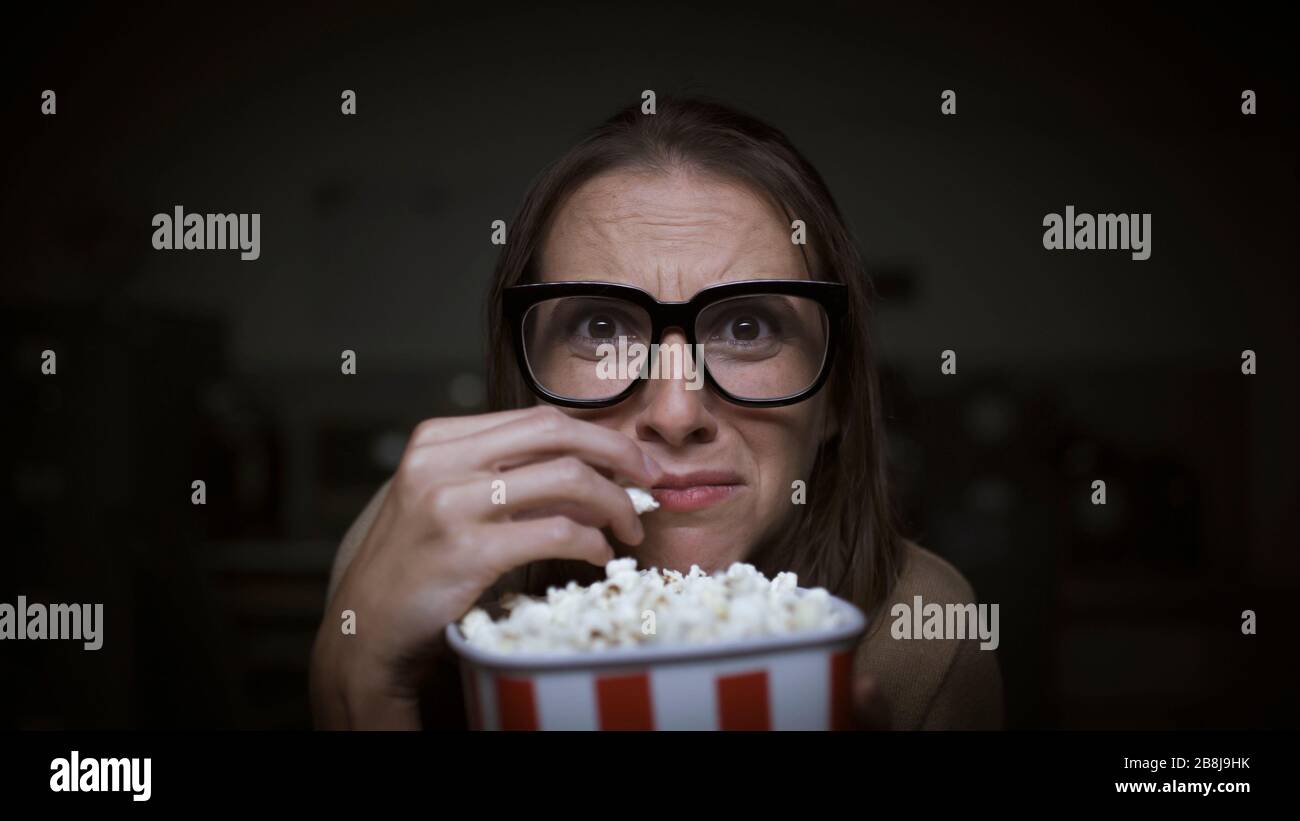 Funny scared woman watching horror movies and eating popcorn at home ...