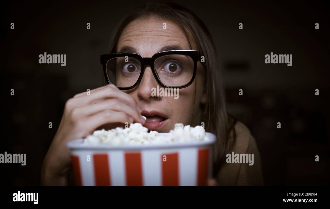 Funny scared woman watching horror movies and eating popcorn at home ...