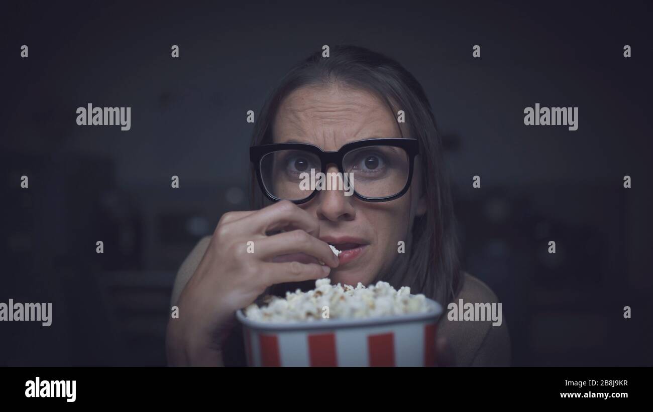 Funny scared woman watching horror movies and eating popcorn at home ...