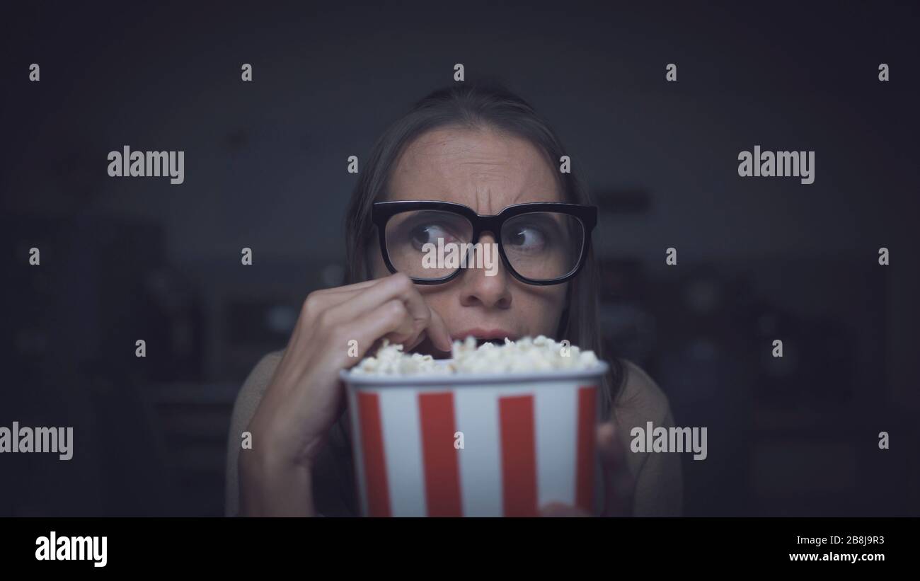 Funny scared woman watching horror movies and eating popcorn at home ...