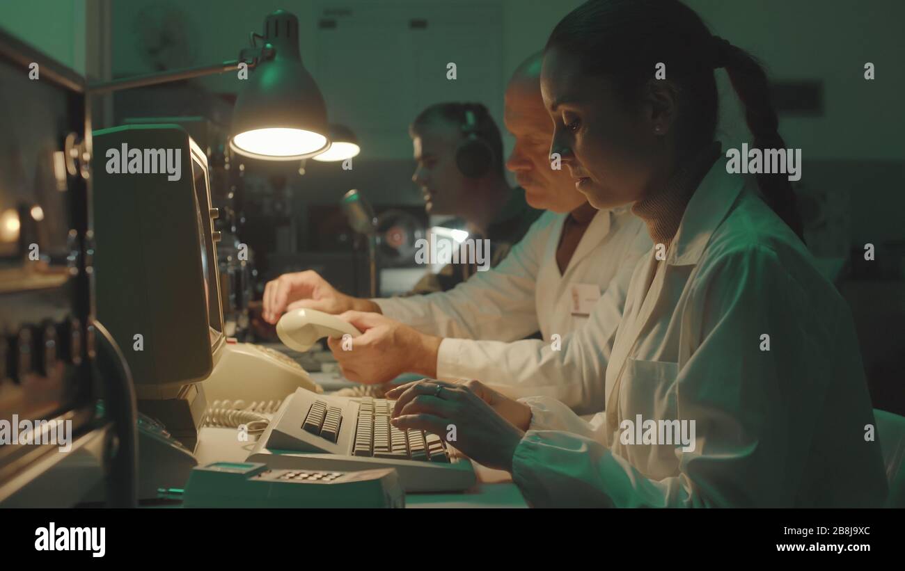 Team of scientists working in a vintage style control room, they are ...