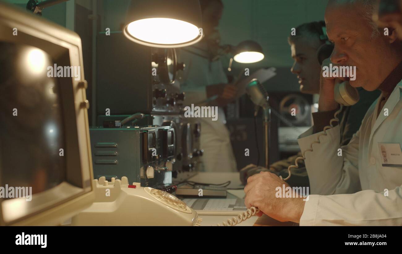 Team of scientists working in a vintage style control room, they are ...