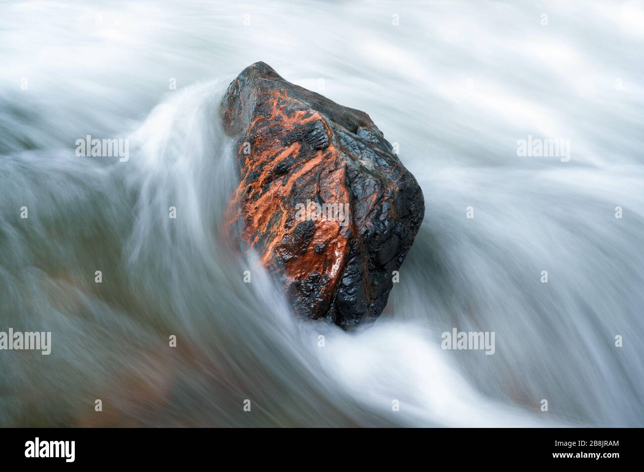 Stone in a stream with water blurred by long exposure Stock Photo - Alamy
