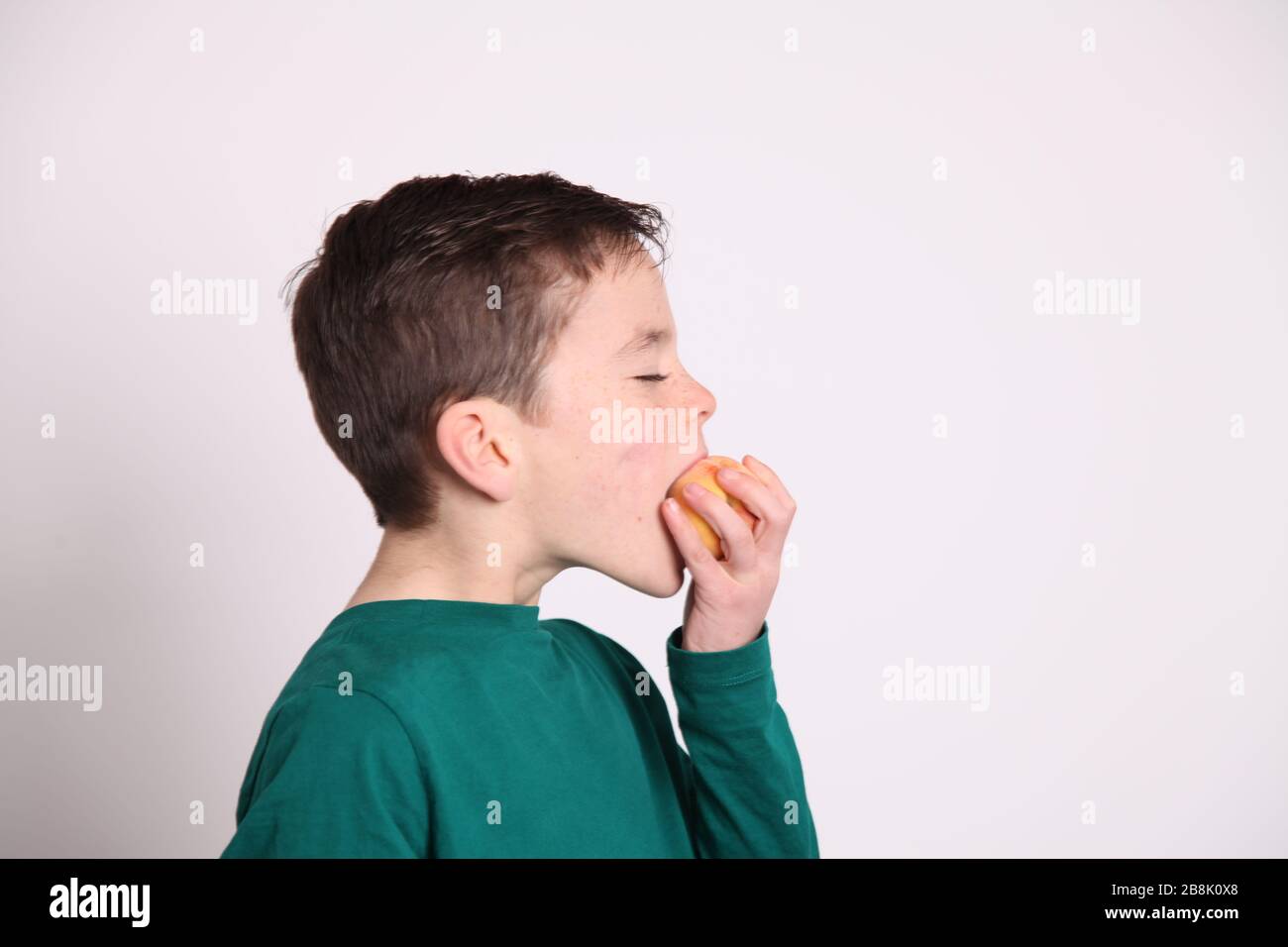 A young boy aged 8 years old eating biting a peach fruit, UK 2020 Stock ...