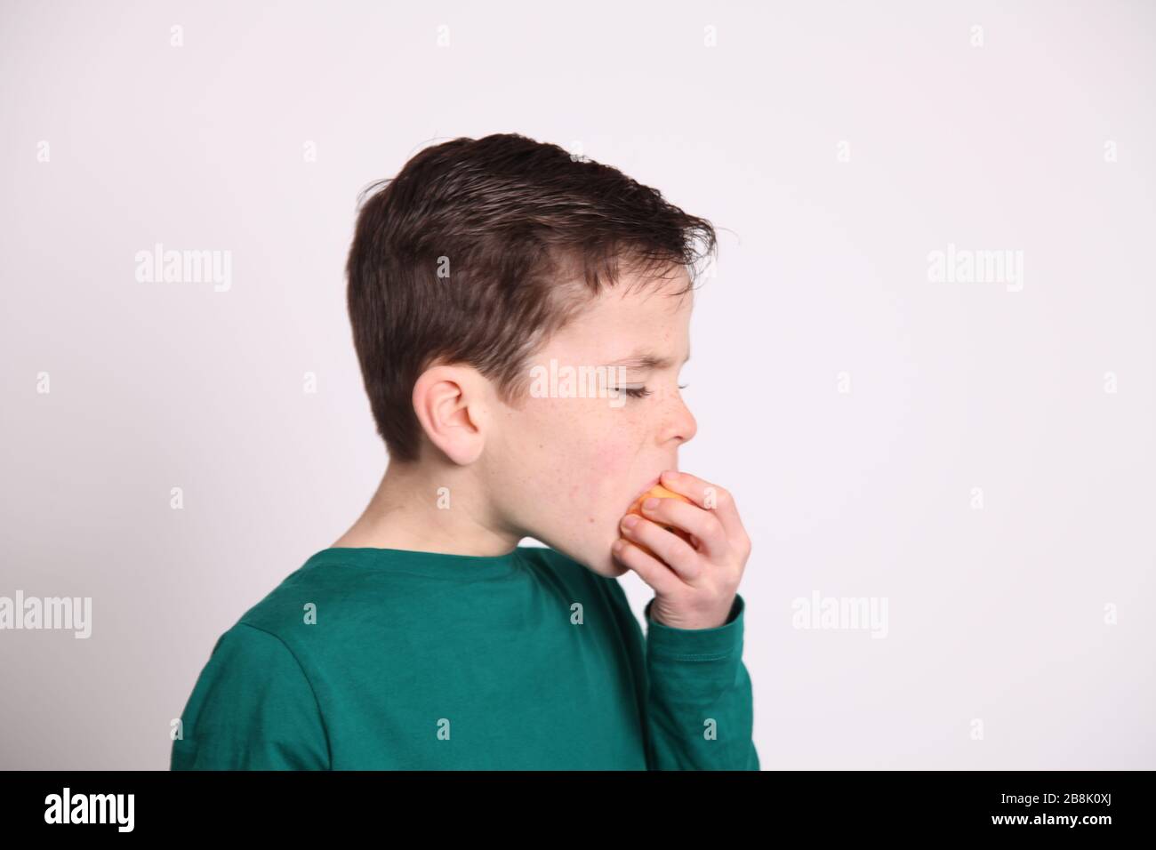 A young boy aged 8 years old biting into a peach fruit, UK 2020 Stock ...