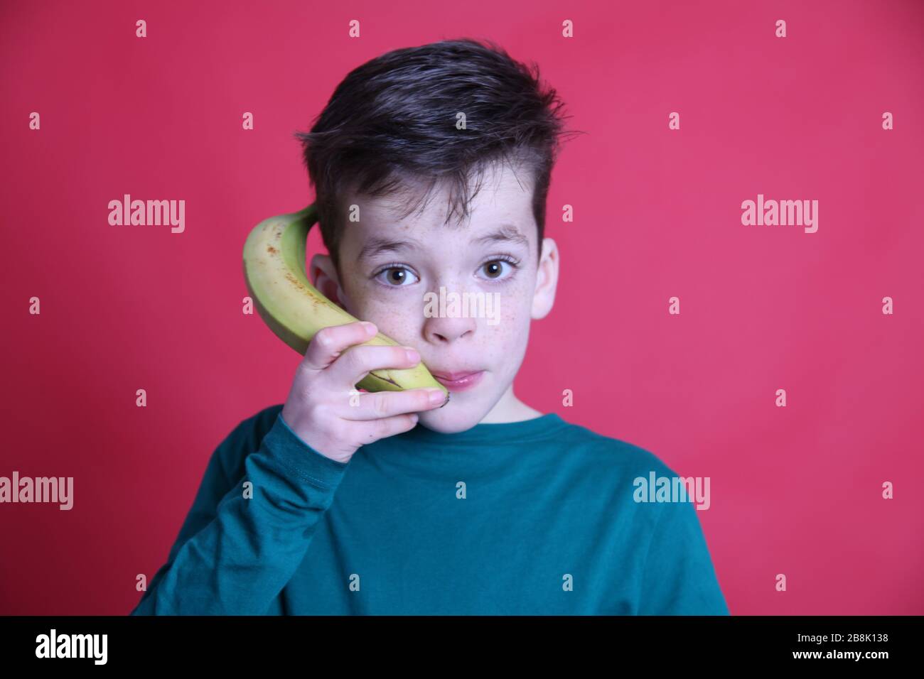 A young boy aged 8 using a banana as a phone, red background, UK 2020 ...