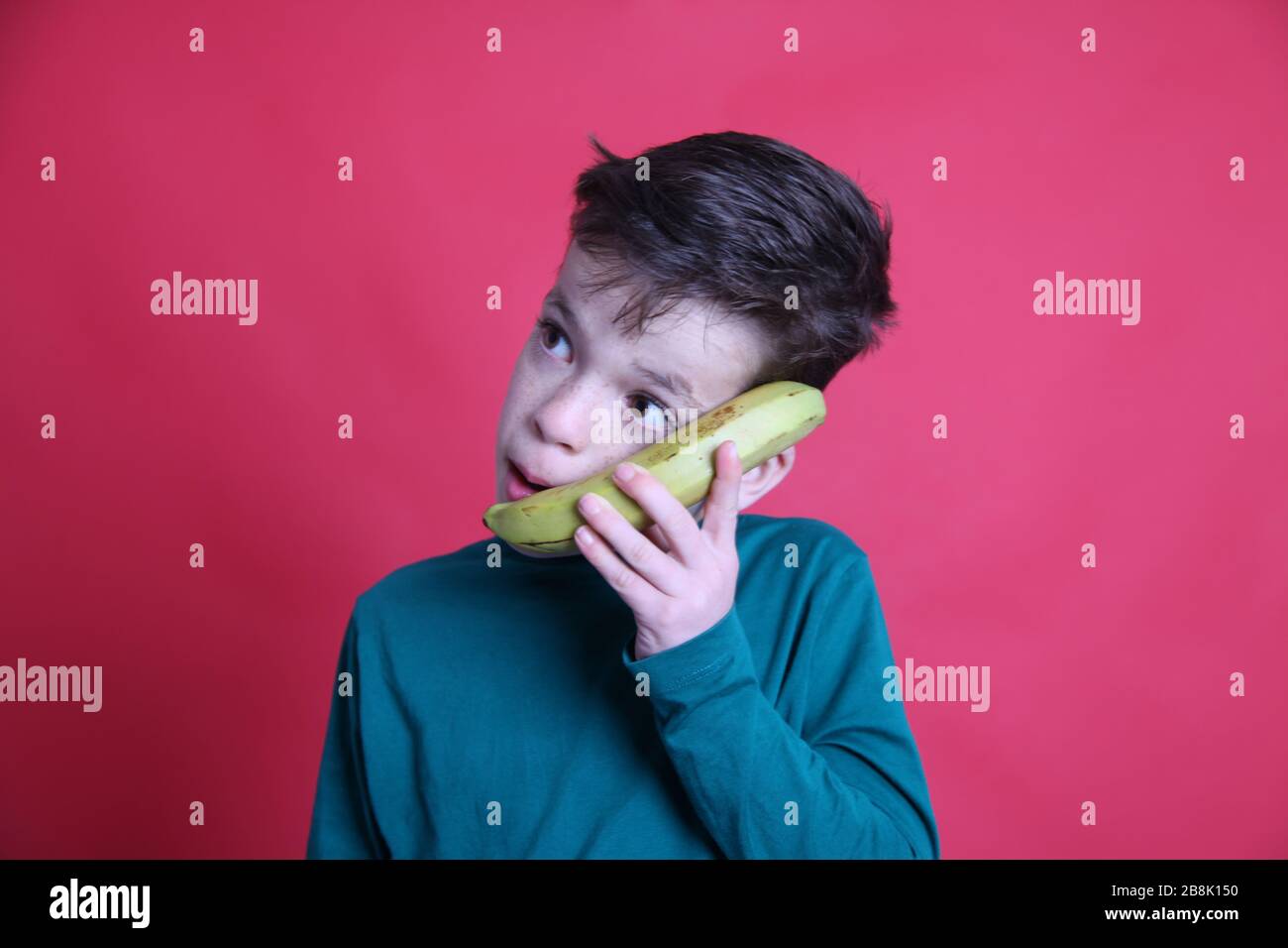 A young boy aged 8 using a banana as a phone, red background, UK 2020 ...