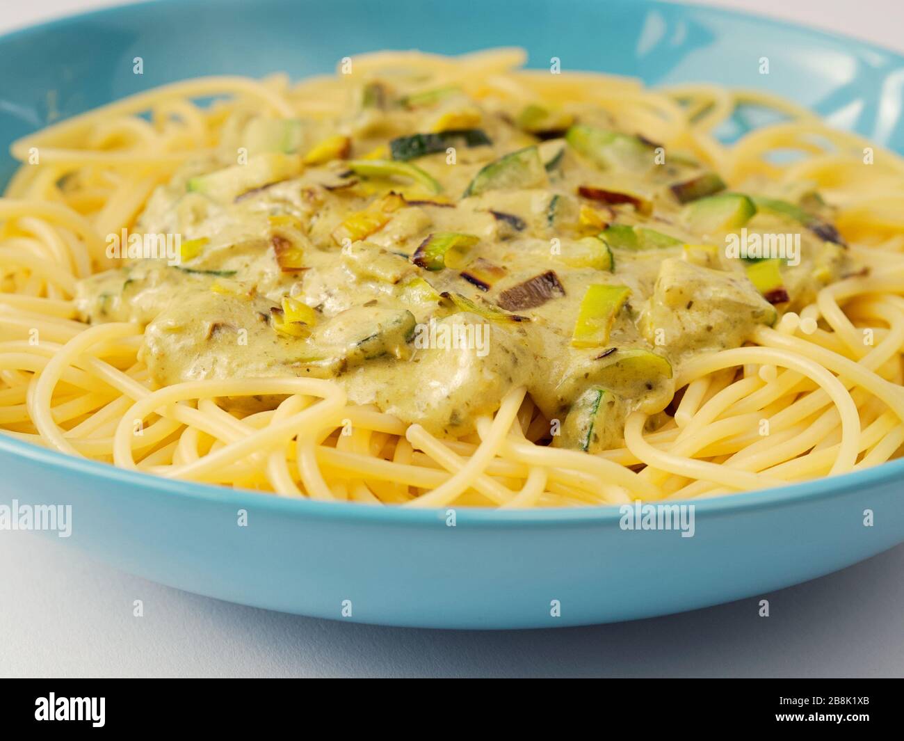 Spaghetti with a cream sauce with zucchini and leek in a light blue ...
