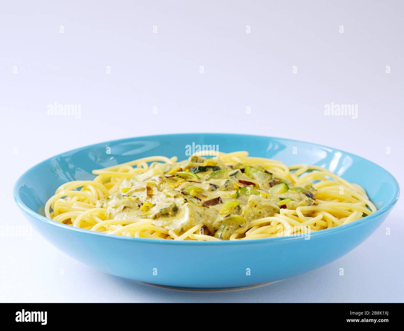 Spaghetti with a cream sauce with zucchini and leek in a light blue ...