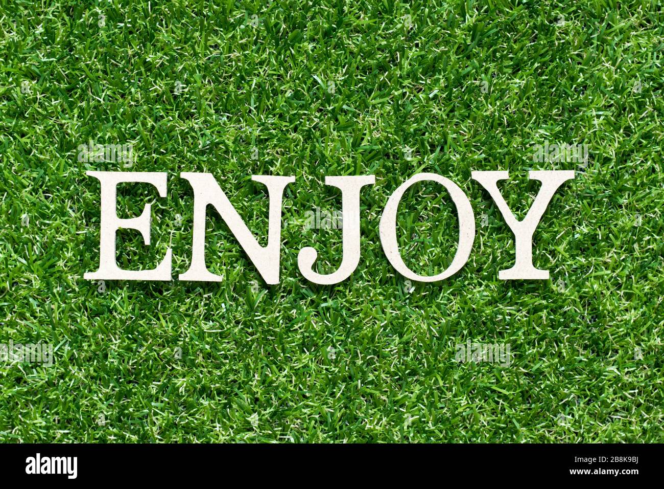 Wood alphabet letter in word enjoy on artificial green grass background ...