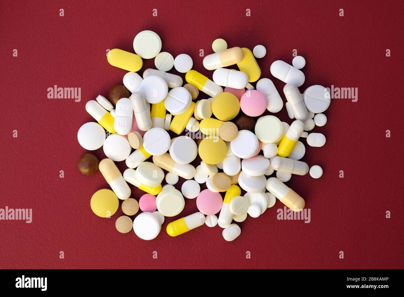 Pills of different shapes and colors on a red background top view. Many ...