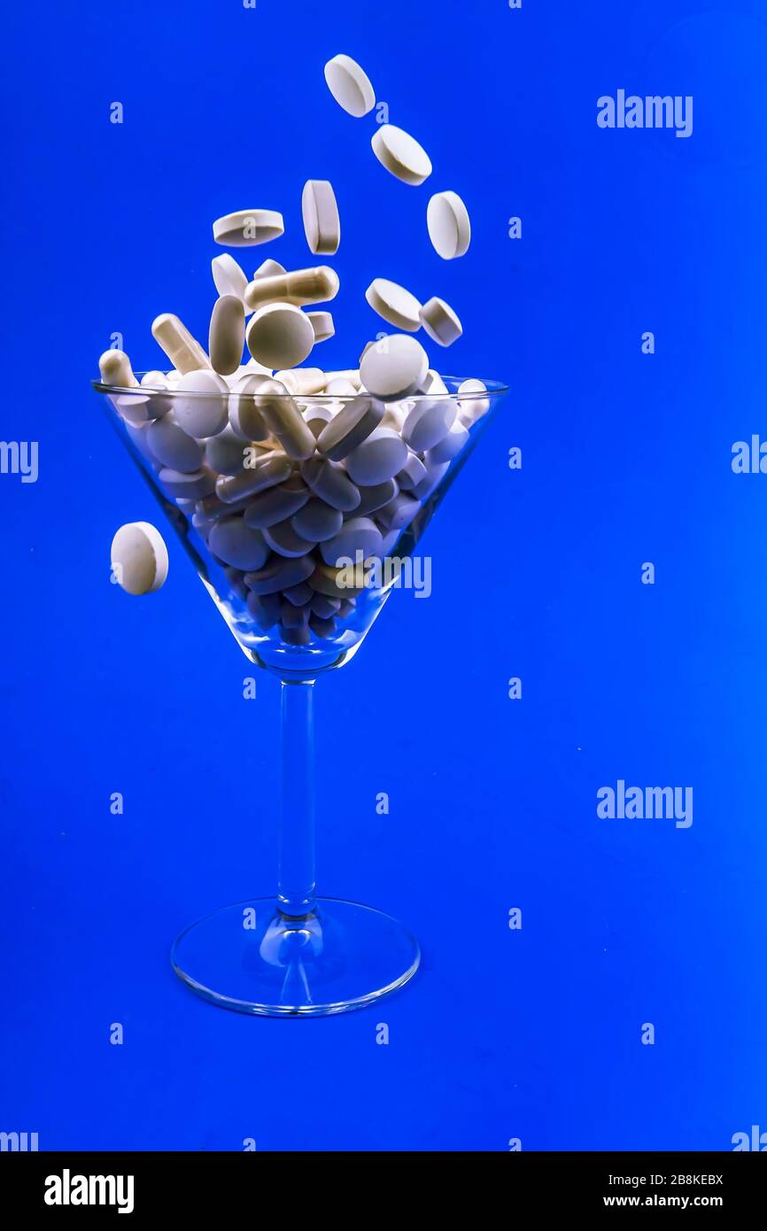 Falling white pills, tablets capsule in a martini glass on blue ...