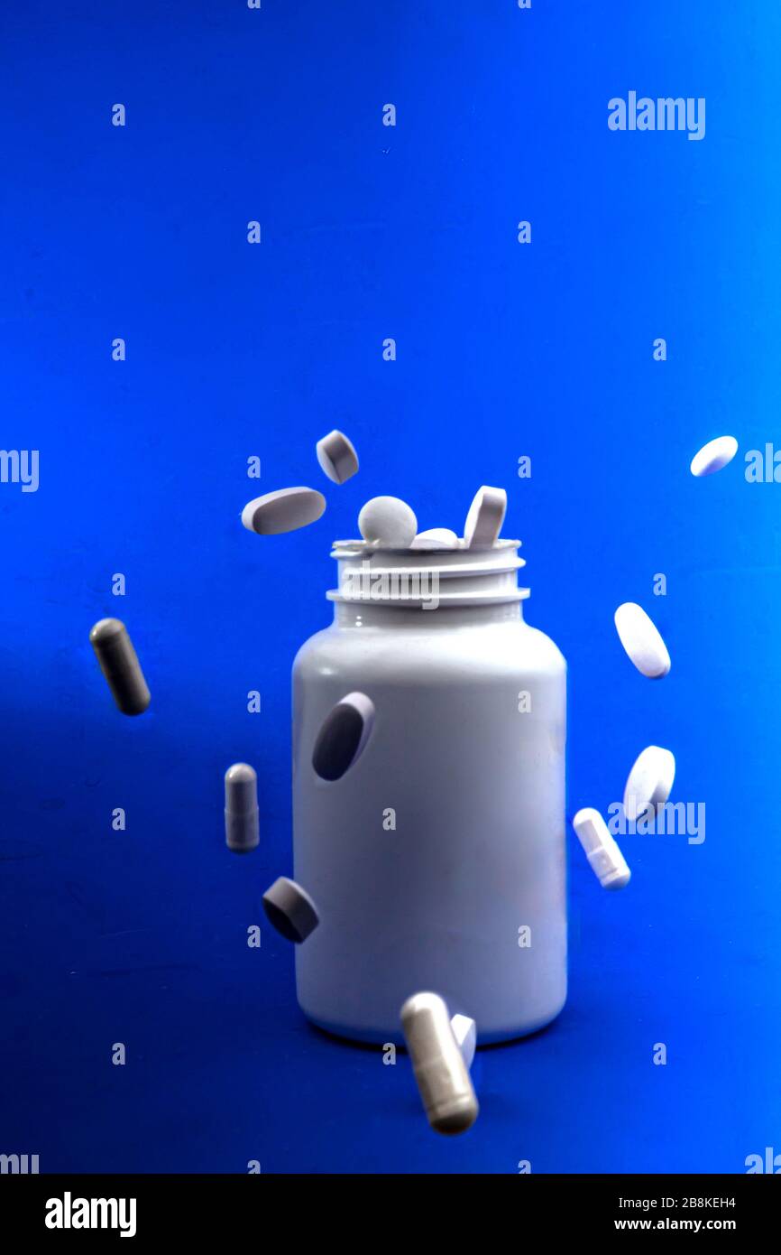 Falling white pills, tablets capsule in a white bottle glass on blue ...
