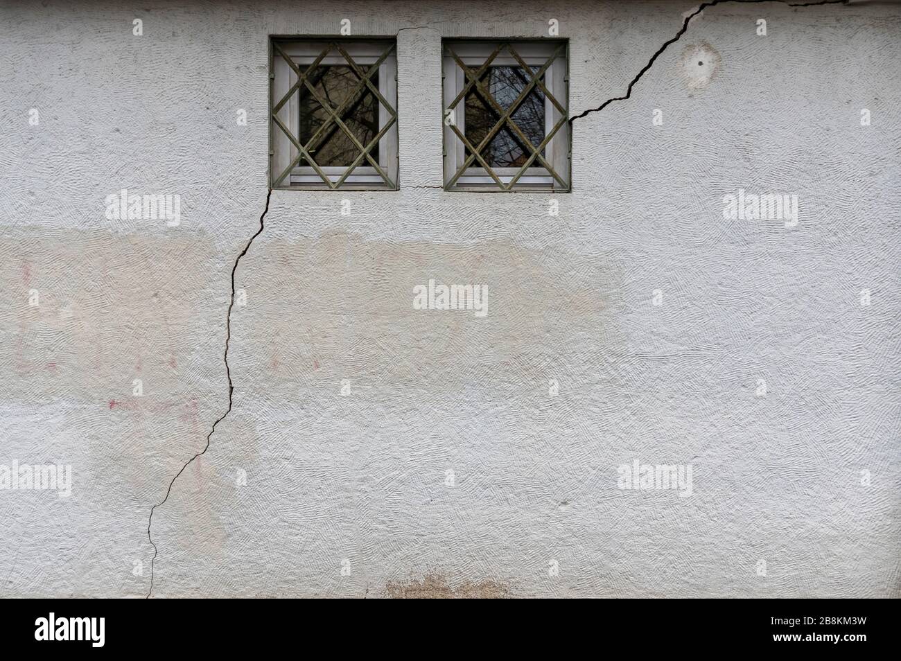 Facade with 2 small, barred windows through which a long and wide crack ...
