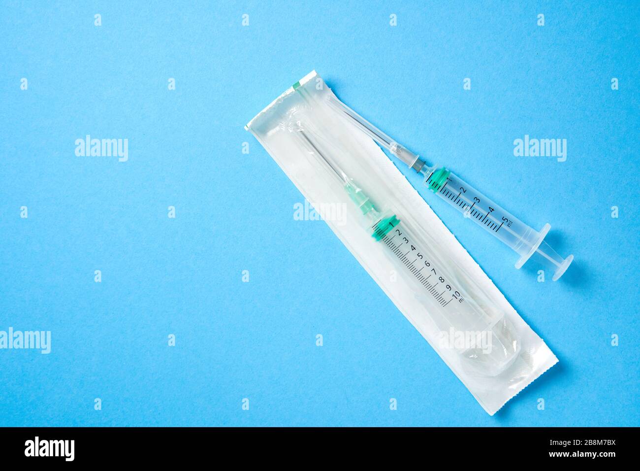 Two plastic disposable medical syringes open and package lie on blue ...