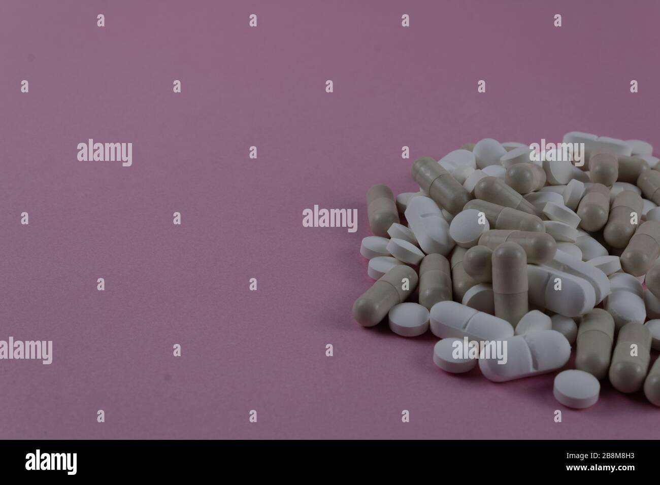 A bunch of colored pills mixed together on a pink background. Mixed ...