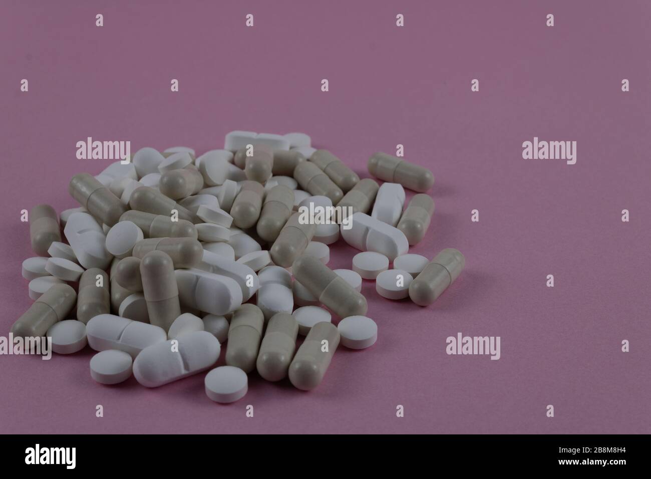 A bunch of colored pills mixed together on a pink background. Mixed ...