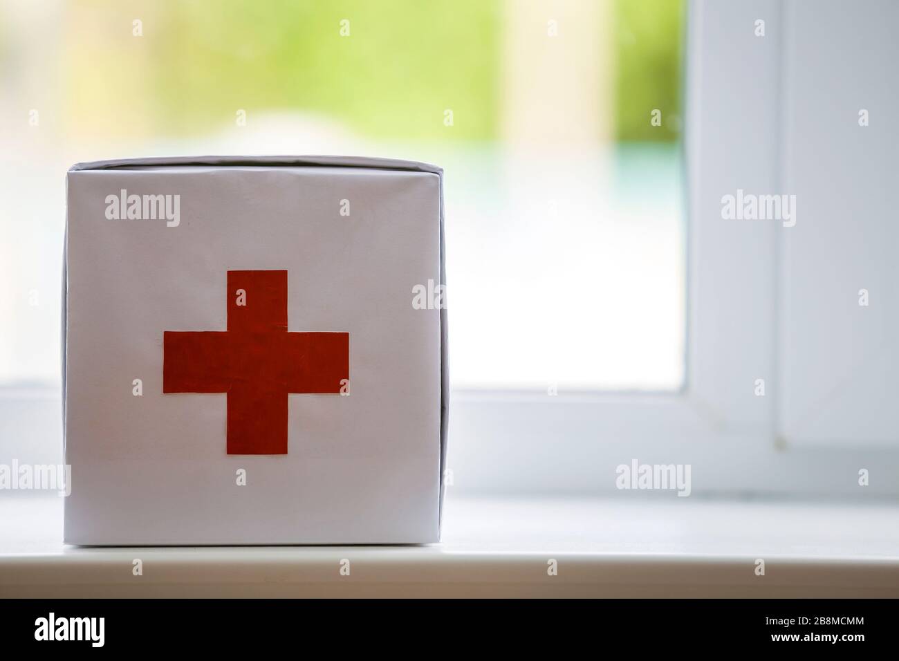 White first aid kit with red cross indoors on windowsill on blurred ...