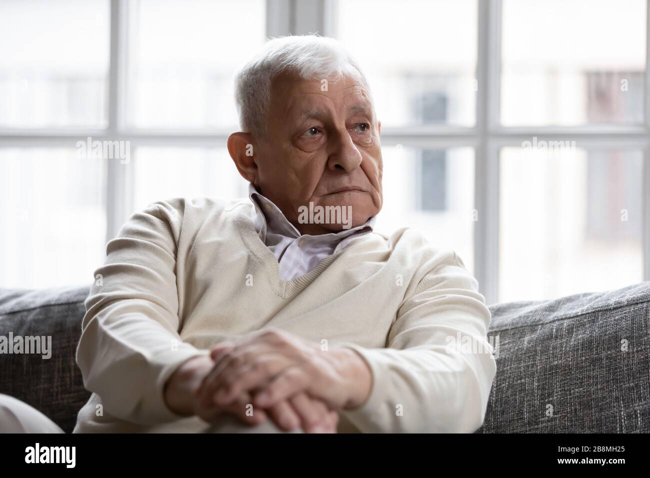Pensive old man sitting on couch in living room alone Stock Photo - Alamy