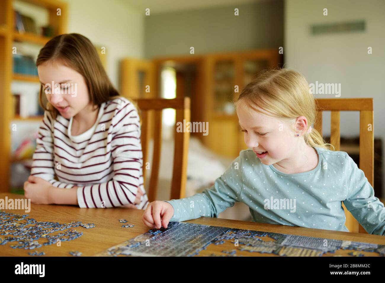 Cute young girls playing puzzles at home. Children connecting jigsaw ...