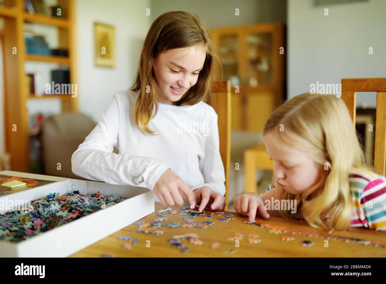Cute young girls playing puzzles at home. Children connecting jigsaw ...