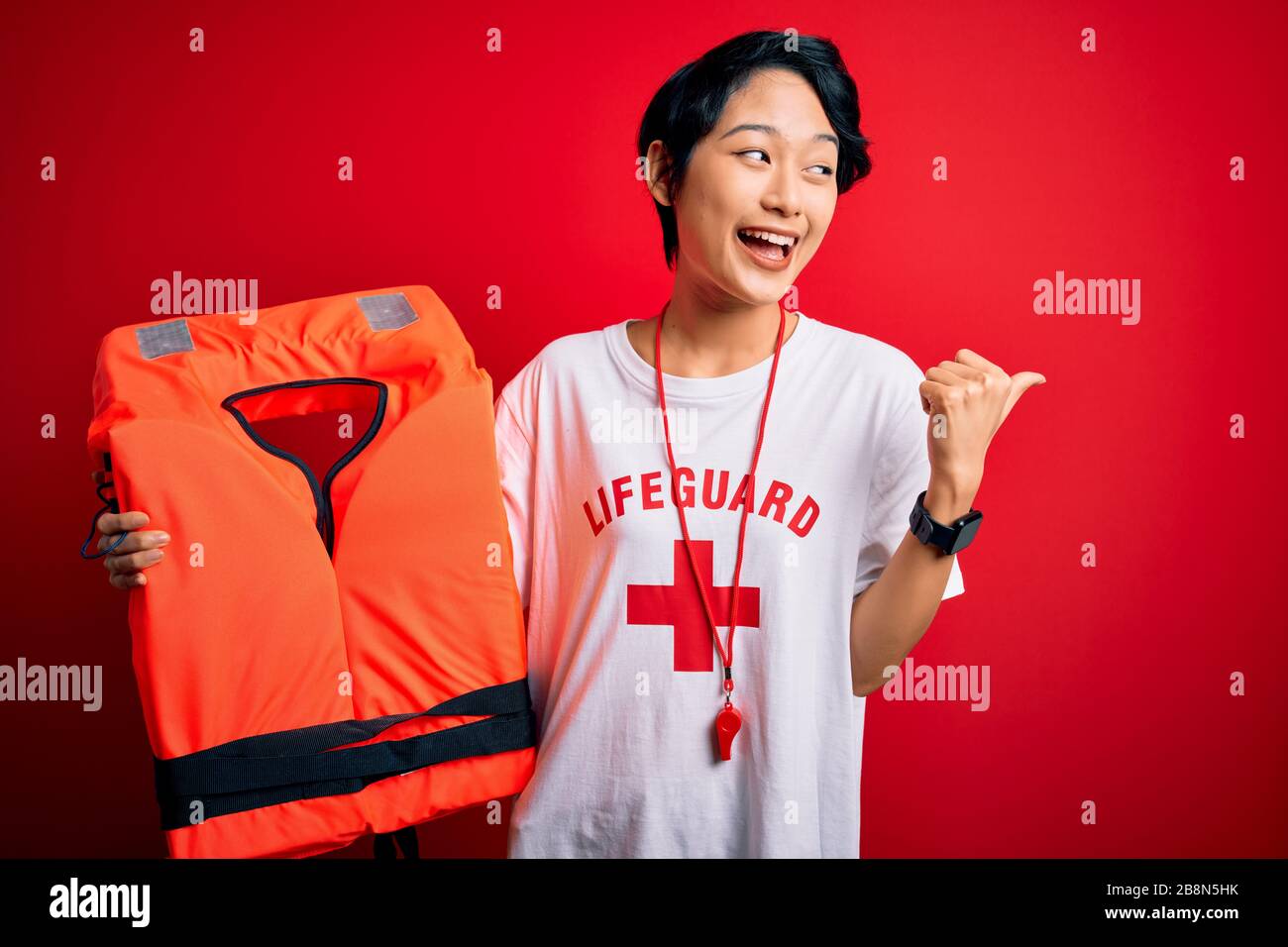 Young beautiful asian lifeguard girl using whistle holding orange life ...