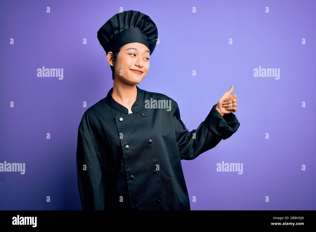 Young beautiful chinese chef woman wearing cooker uniform and hat over ...