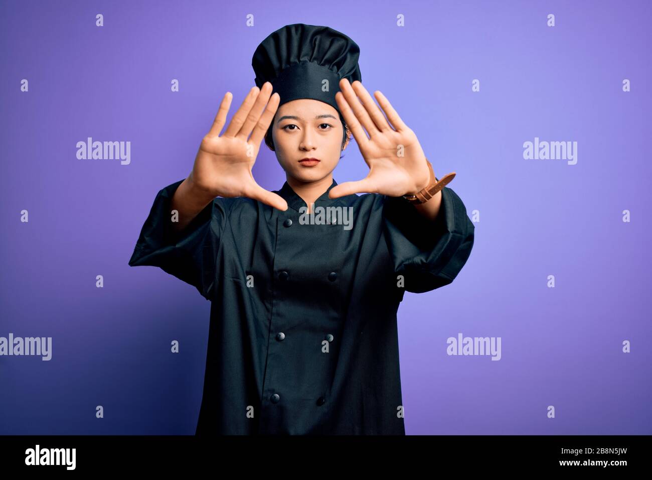 Young beautiful chinese chef woman wearing cooker uniform and hat over ...