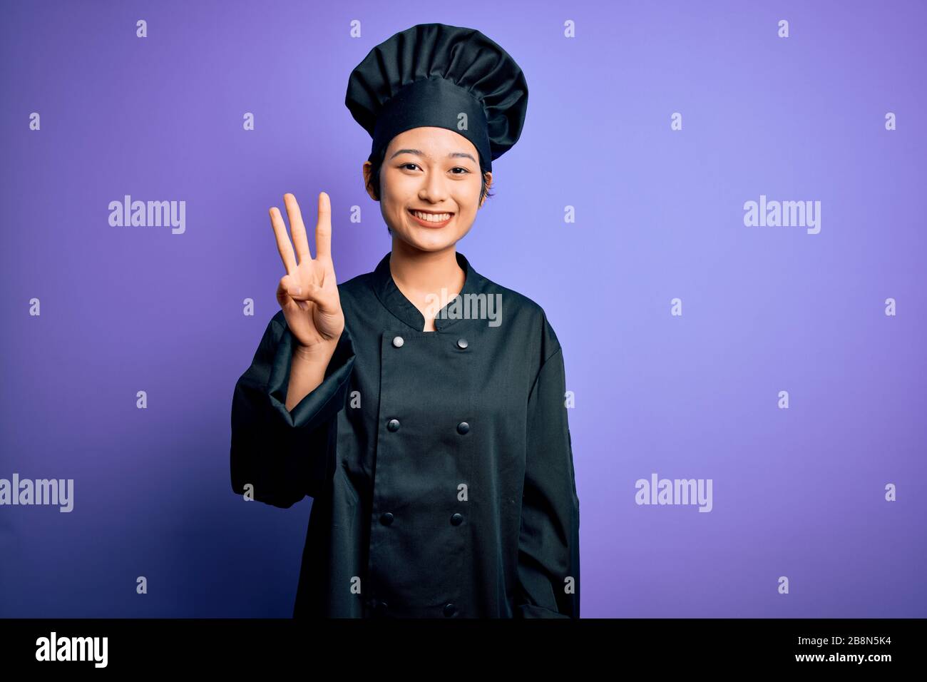 Young beautiful chinese chef woman wearing cooker uniform and hat over ...