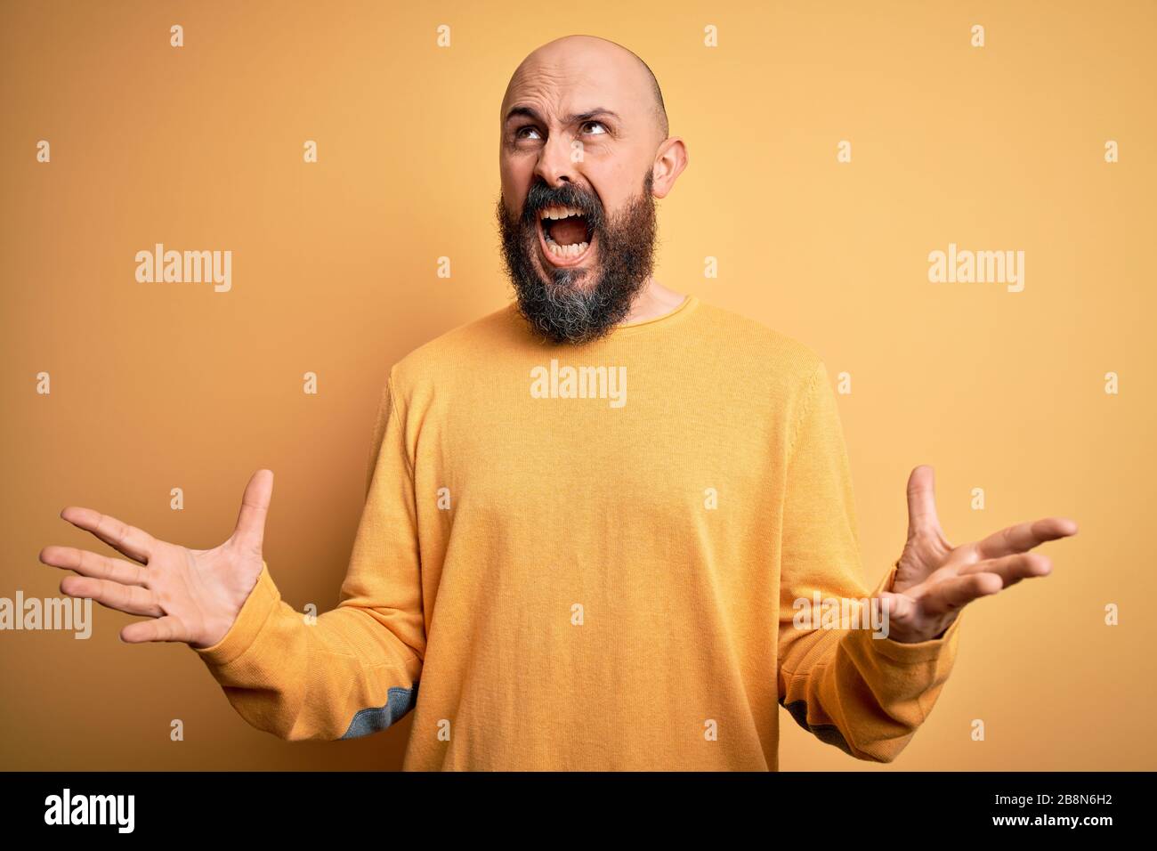 Handsome bald man with beard wearing casual sweater standing over ...
