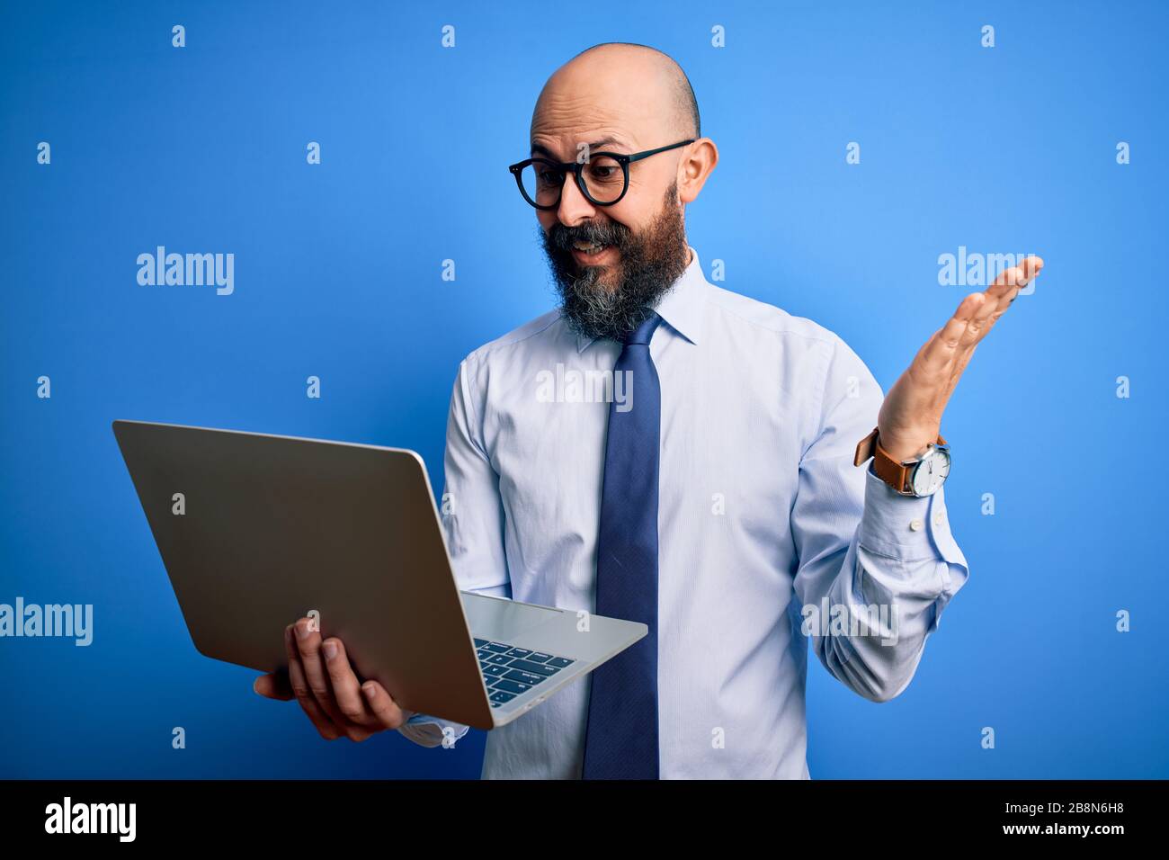 Handsome bald business man with beard working using laptop over blue ...