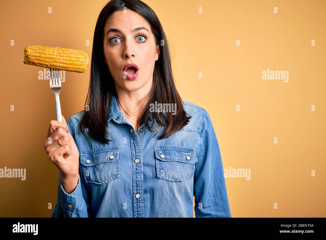 Young woman with blue eyes holding fork with fresh cob corn standing ...