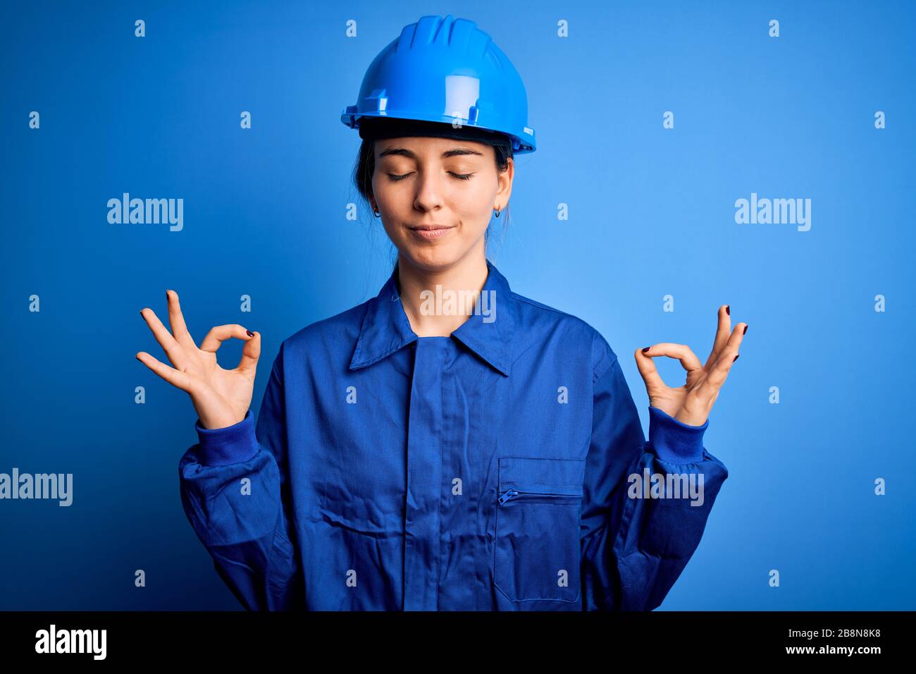 Young beautiful worker woman with blue eyes wearing security helmet and ...