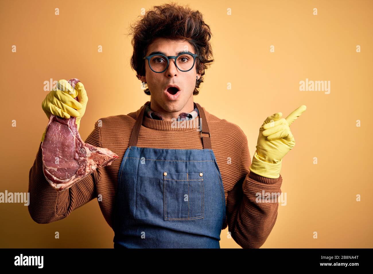Young handsome butcher man holding meet steak standing over isolated ...
