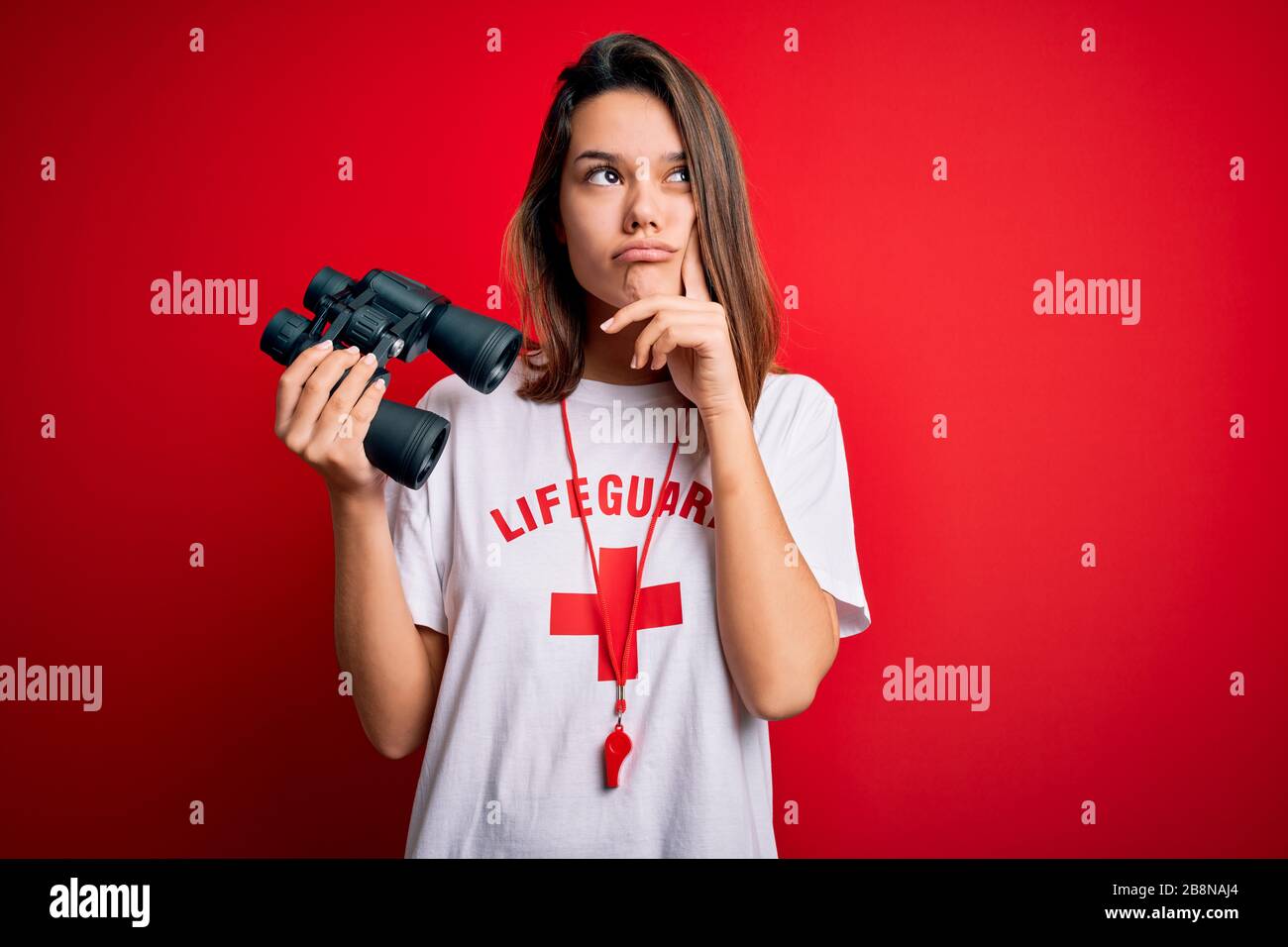 Young beautiful lifeguard girl wearing whistle using binoculars over ...