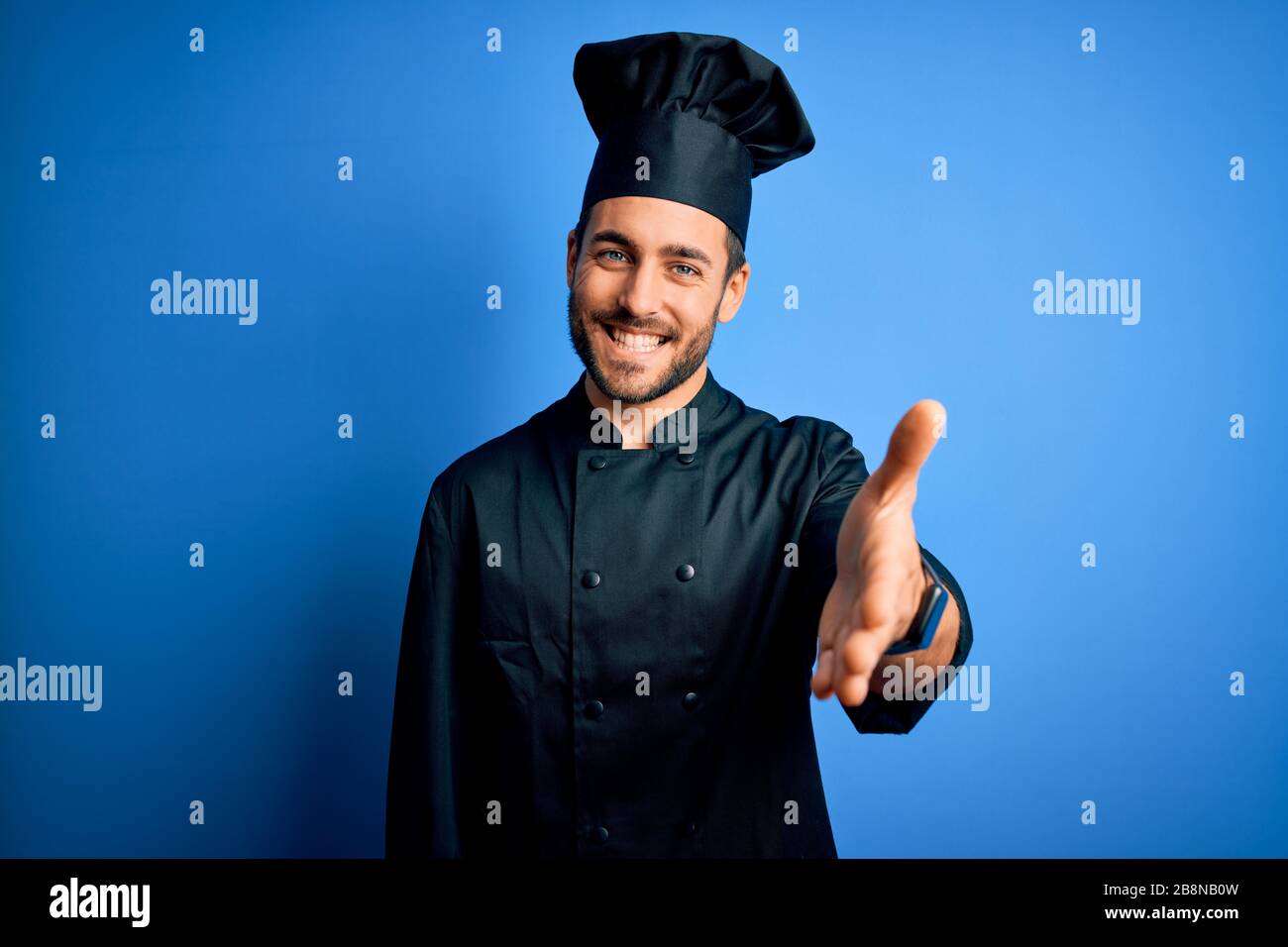 Young handsome chef man with beard wearing cooker uniform and hat over ...