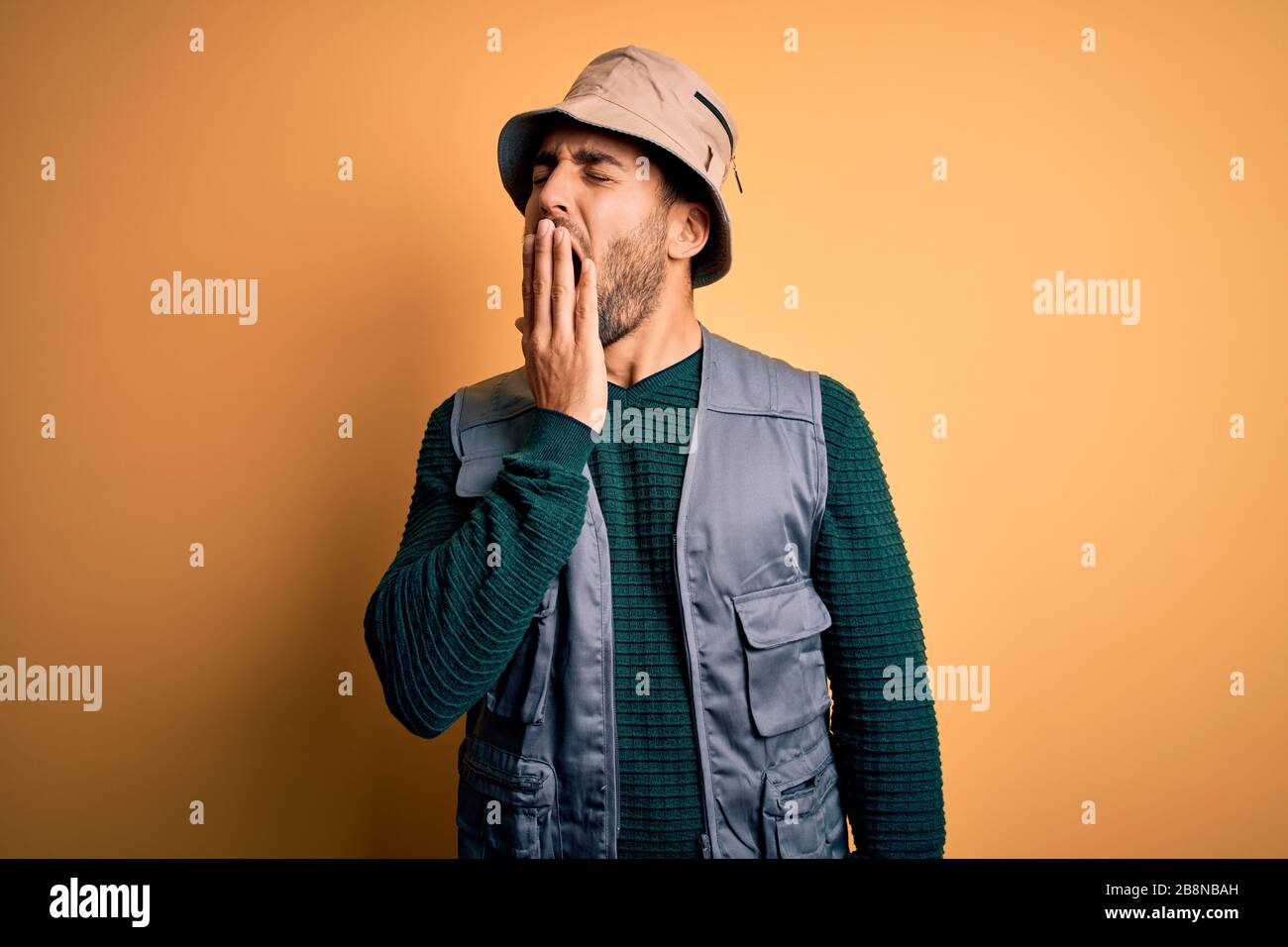 Handsome tourist man with beard on vacation wearing explorer hat over ...