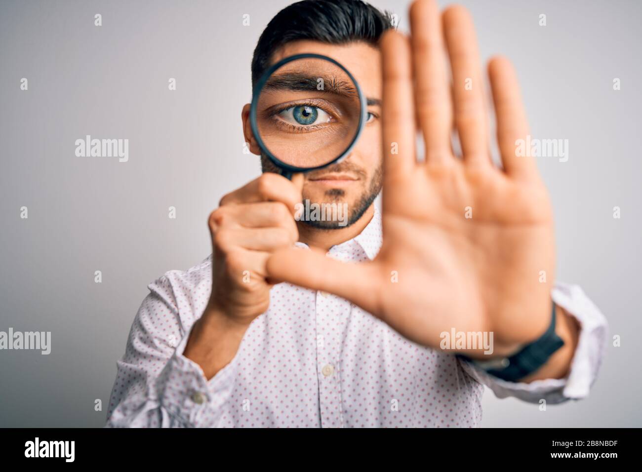 Young detective man looking through magnifying glass over isolated ...
