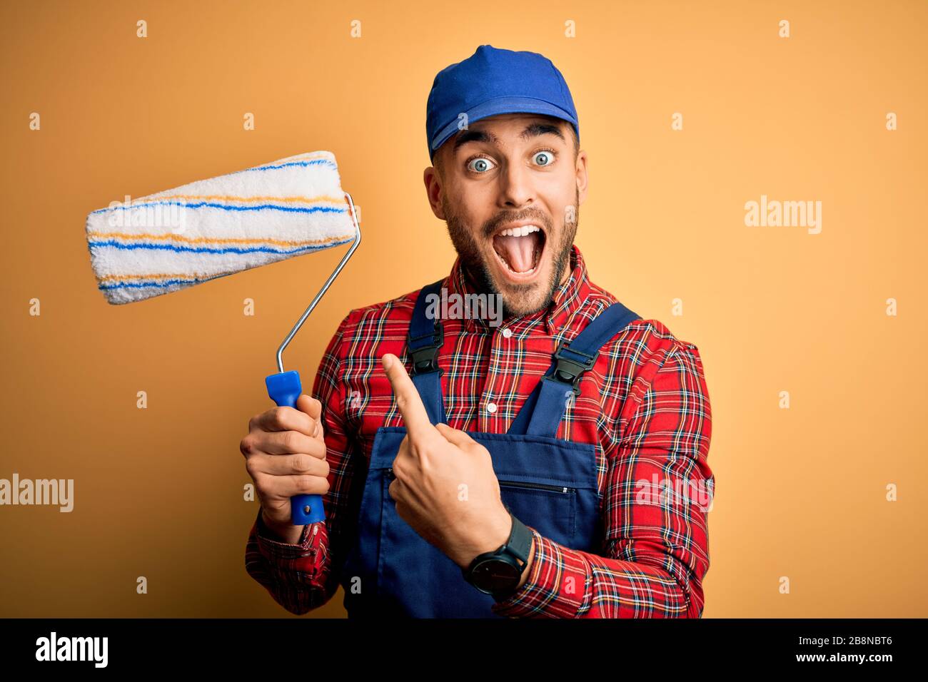 Young handsome painter man painting wall using roller over isolated ...