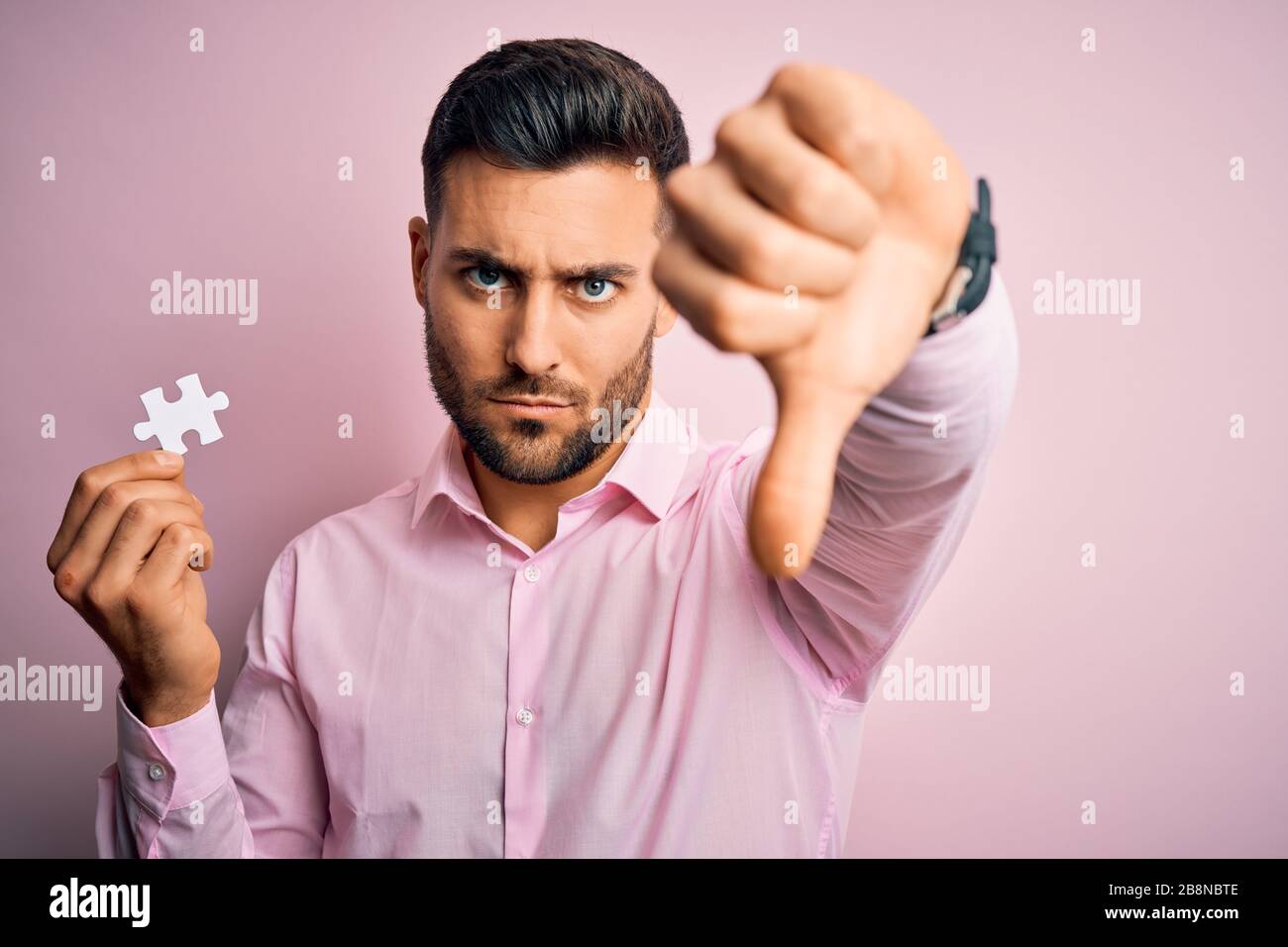 Young handsome businessman holding piece of puzzle over isolated pink ...