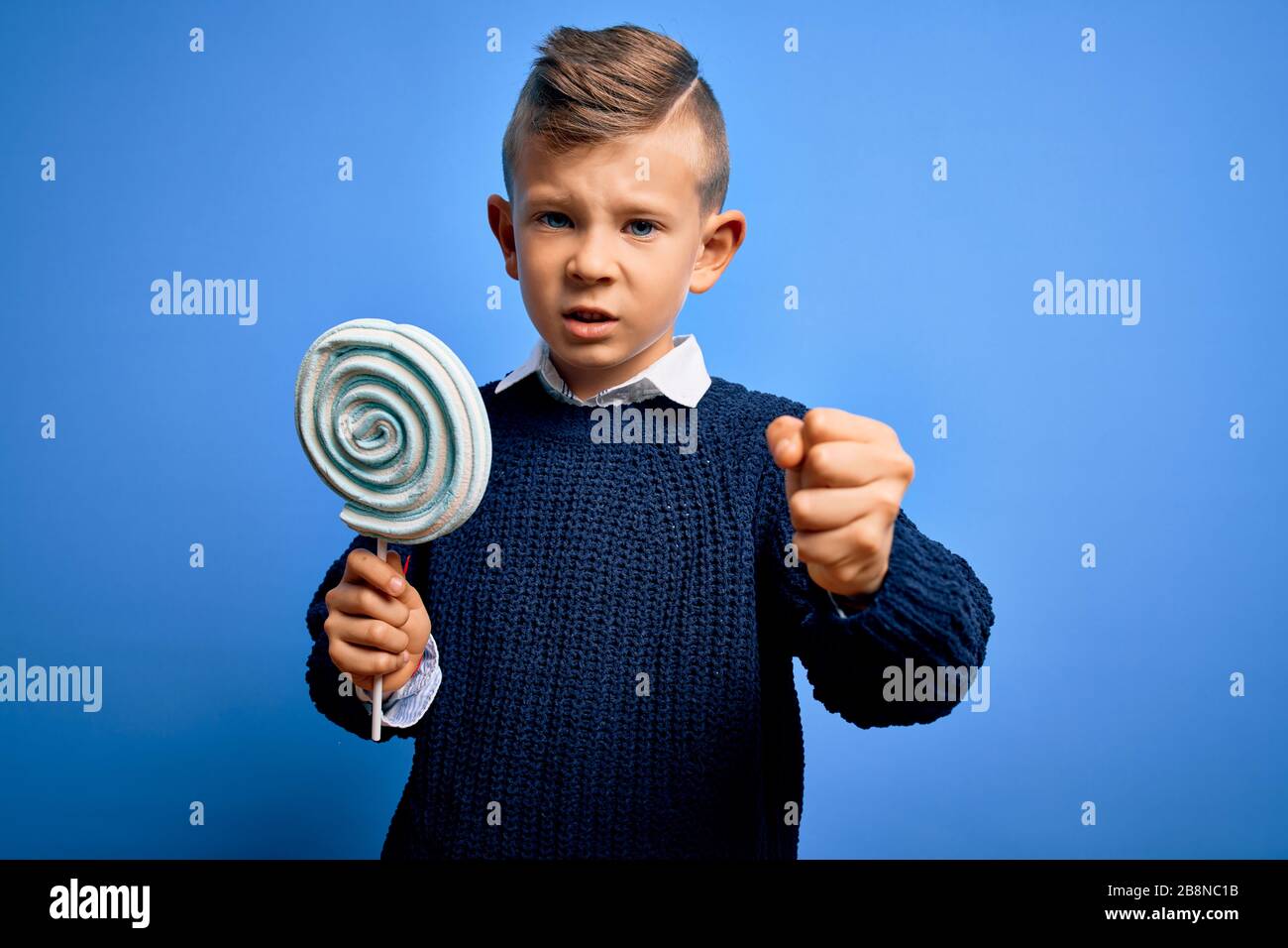 Young little caucasian kid eating sweet candy lollipop over blue ...