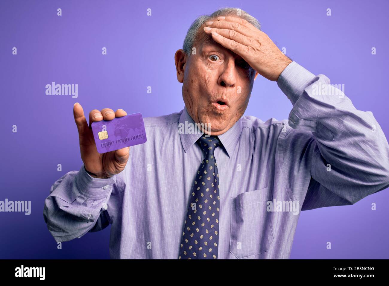 Senior grey haired business man holding credit card over purple ...