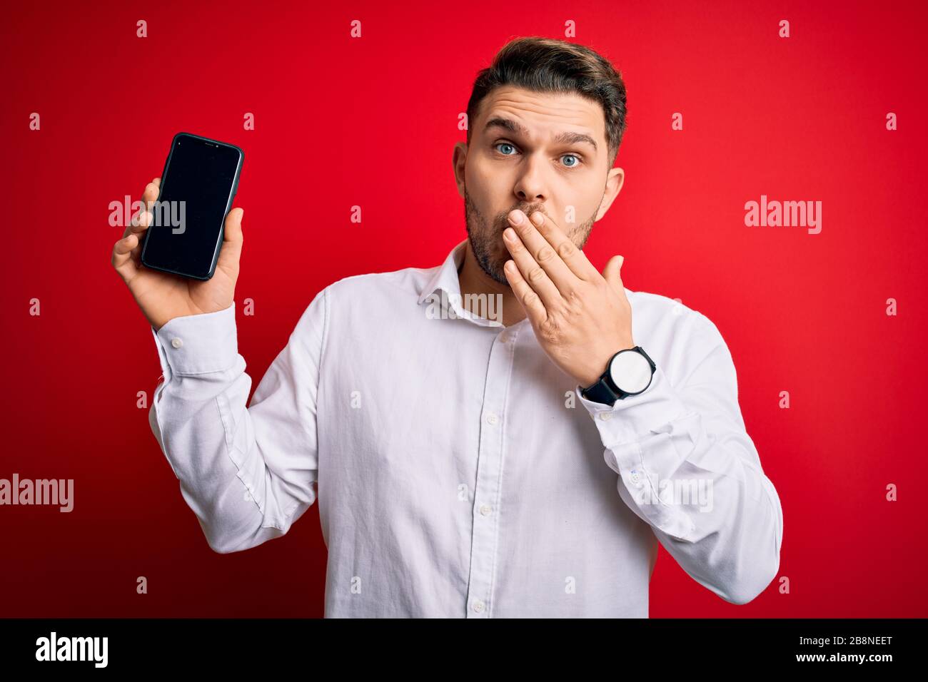 Young business man with blue eyes showing smartphone screen over red ...