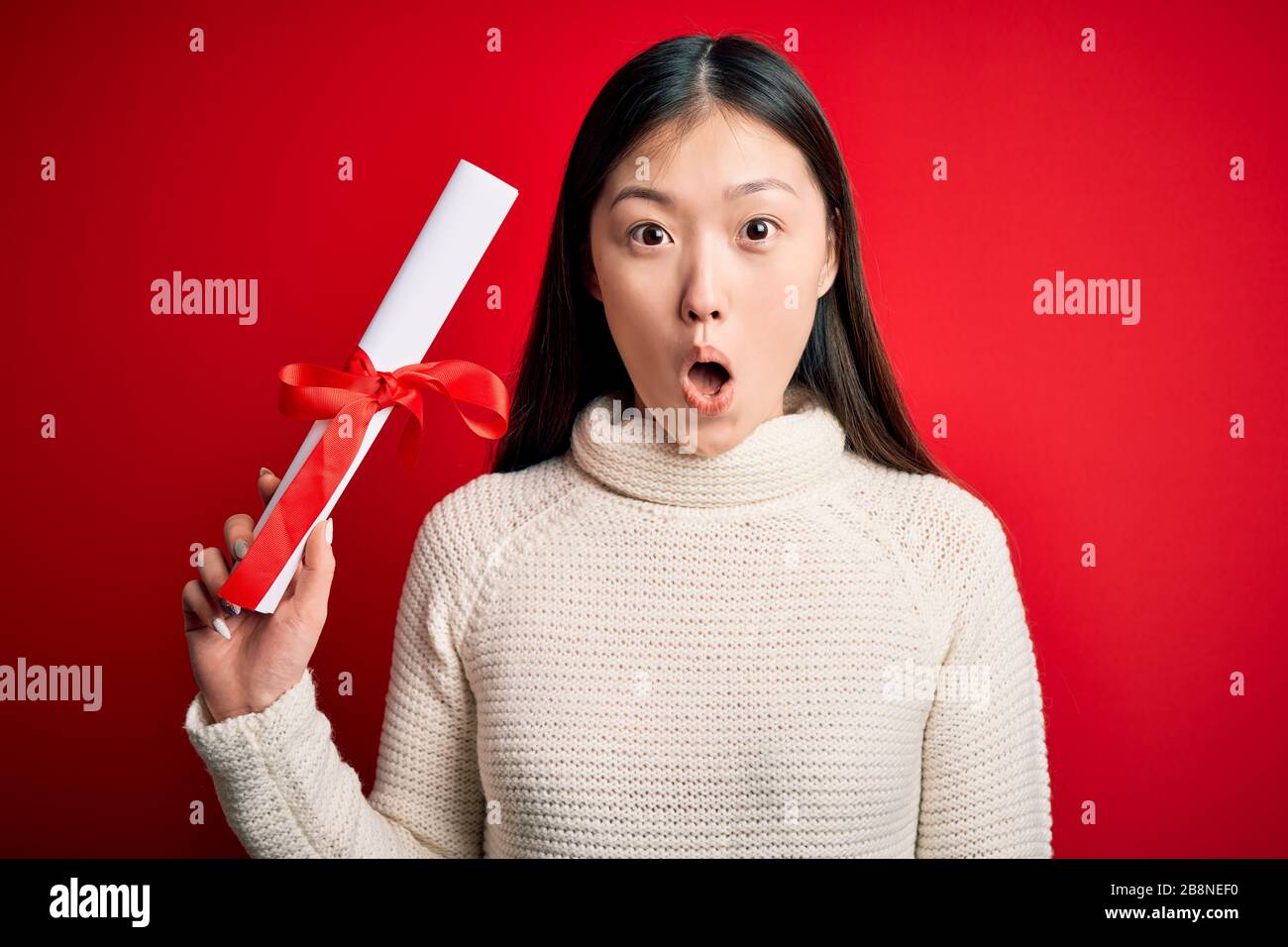 Young asian student woman holding graduate diploma over red isolated ...