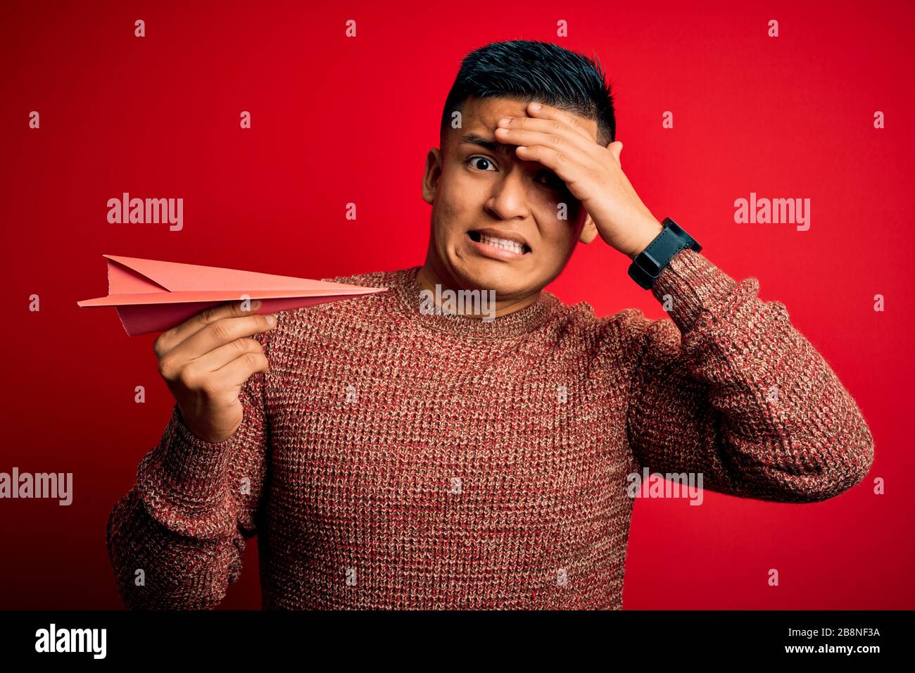 Young handsome latin man holding paper plane over isolated red ...