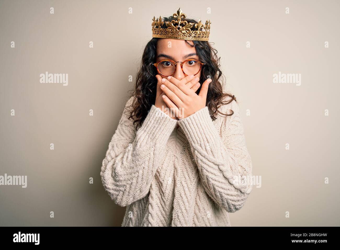 Young beautiful woman with curly hair wearing golden queen crown over ...