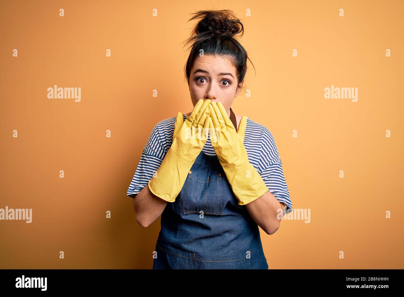 Young brunette cleaner woman wearing housekeeping gloves over yellow ...