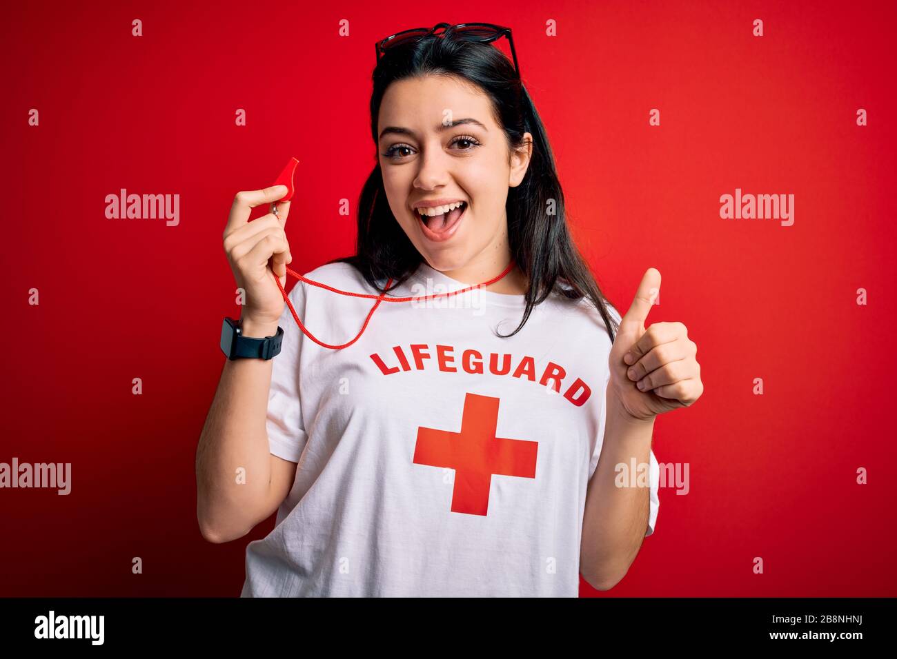 Young lifeguard woman wearing guard equipement holding whistle over red ...